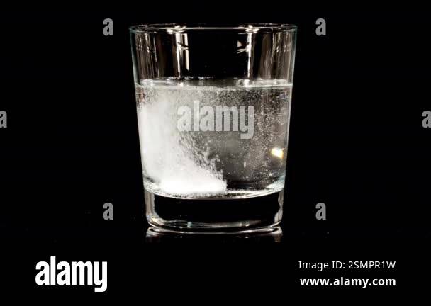 Pill aspirin falling down in glass with water on black background ...