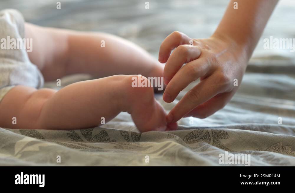 A close-up shot of a mother’s hand gently stroking the tiny toes of her ...