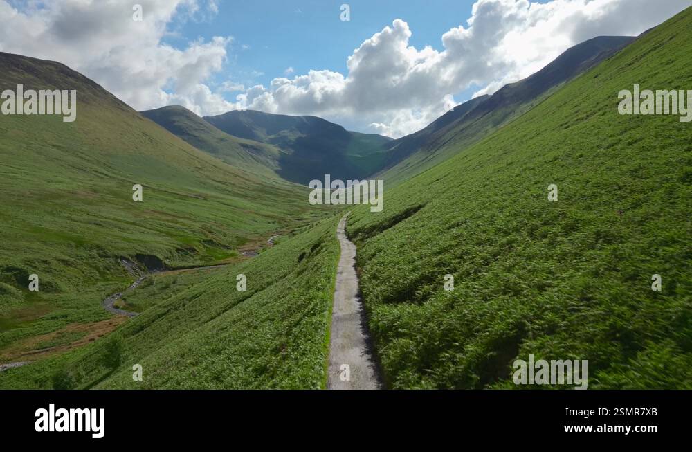Flying low along green valley track with drone rise showing deeper ...