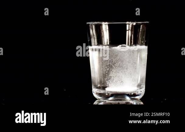 Pill aspirin falling down in glass with water on black background ...
