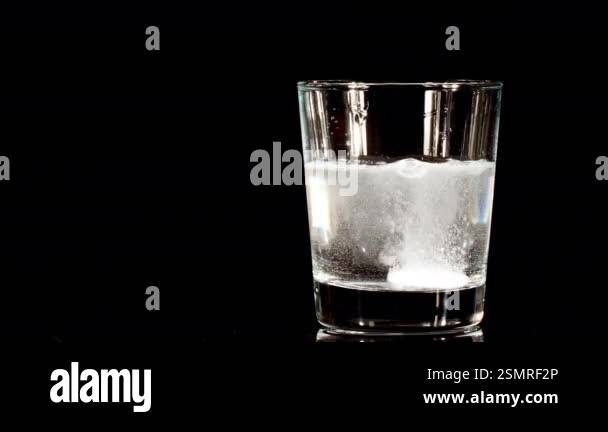 Pill aspirin falling down in glass with water on black background ...