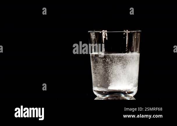 Pill aspirin falling down in glass with water on black background ...