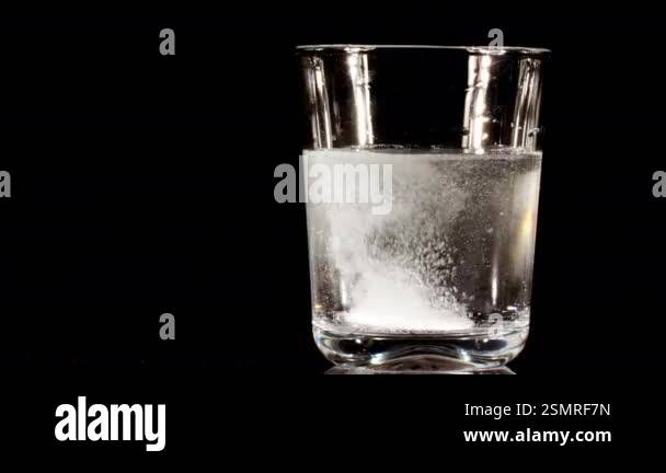 Pill aspirin falling down in glass with water on black background ...