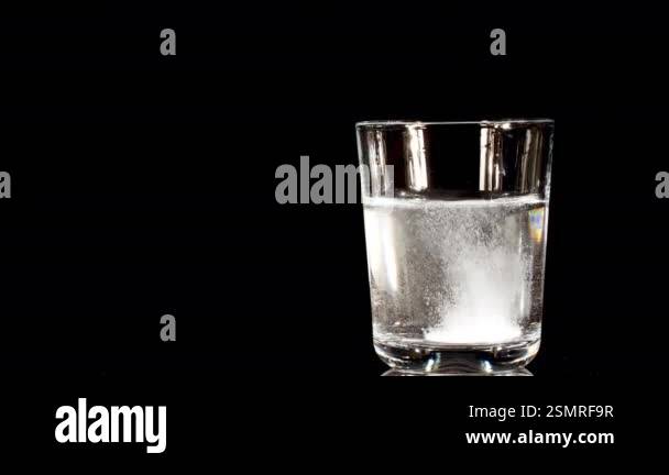 Pill aspirin falling down in glass with water on black background ...