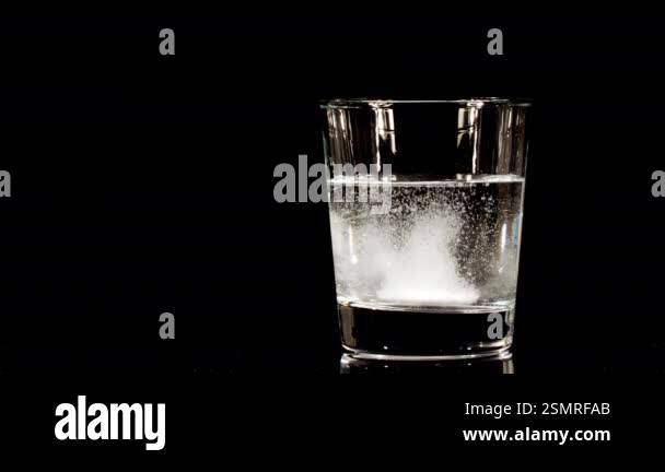 Pill aspirin falling down in glass with water on black background ...