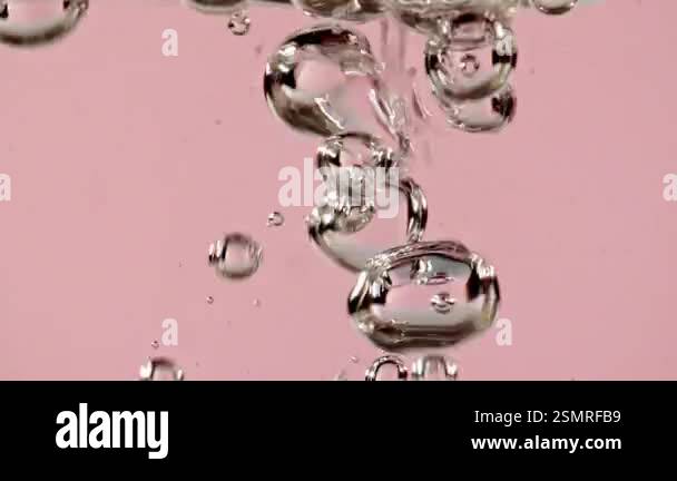 Macro shot of air bubbles in water rising up on light pink background ...