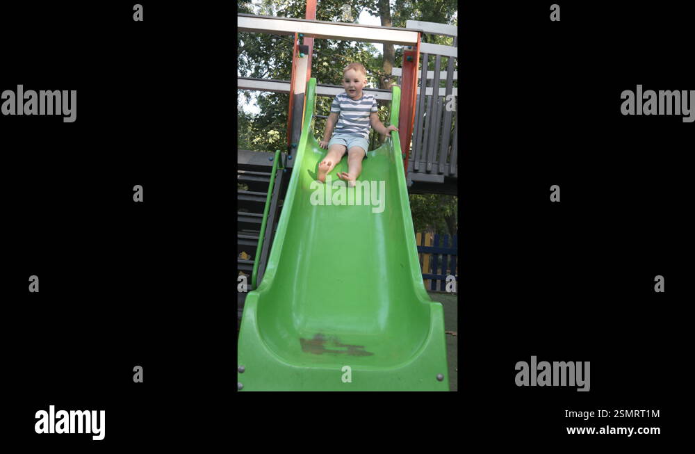 A delighted little boy slides down a plastic slide at a playground ...