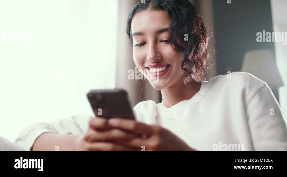Young Asian Lady Smiling While Texting on Her Phone in a Cozy Living ...