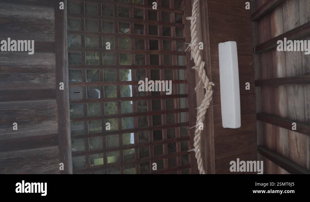 A vertical shot of an old Japanese window with rope above it. An ...