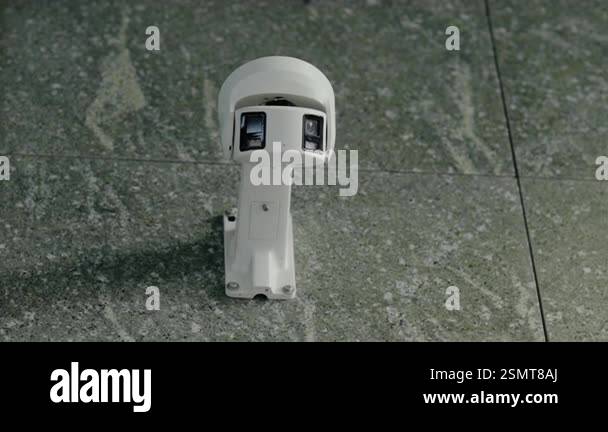 Security camera mounted on a wall. The camera is white and has two ...