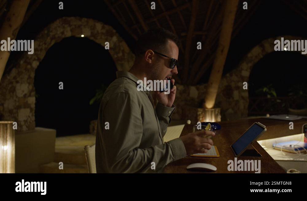 Man wearing shades at night, having exciting phone talk while drinking ...
