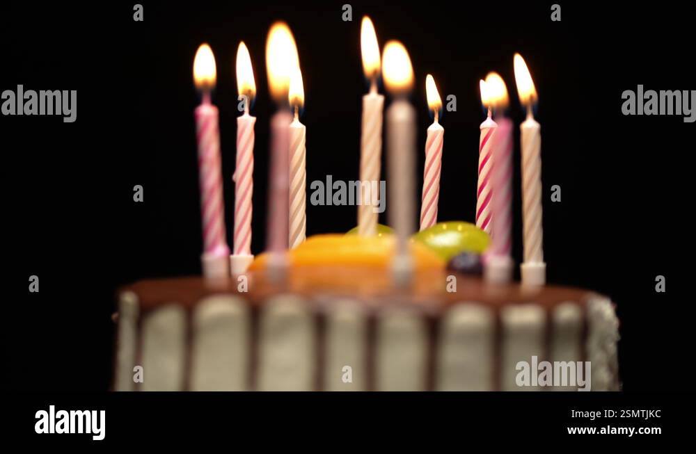 A rotating chocolate-covered birthday cake adorned with lit candles is ...