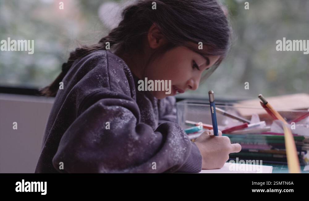 A smiling little girl at her desk, drawing on a piece of paper with a ...