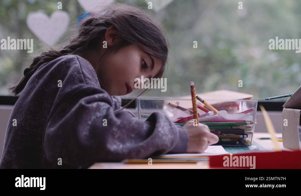 A happy little girl at her desk, drawing with a pencil on a piece of ...
