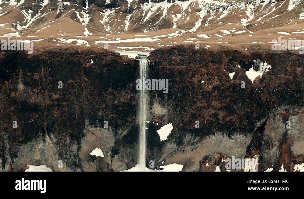 Tilt-Down Aerial of Tall Glacial Waterfall Cascading Off Large Frozen ...