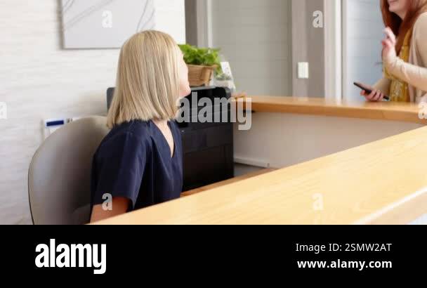 Smiling woman sitting at reception desk in medical clinic, looking at ...