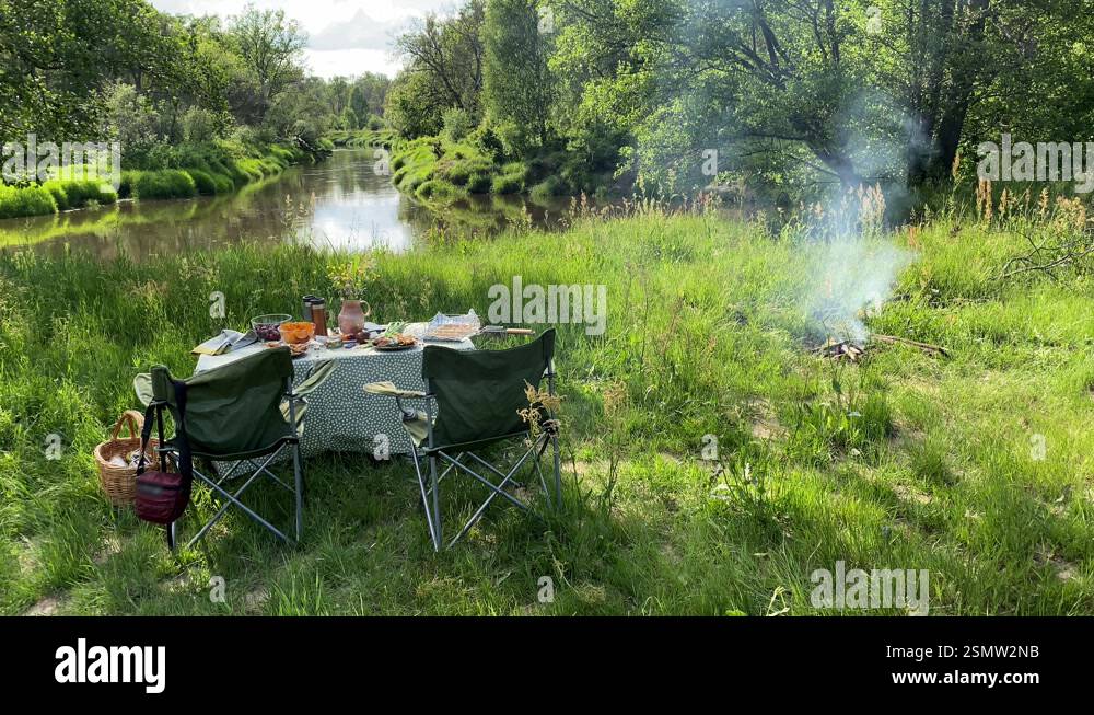 Set picnic table with food and a fire on the bank by the river Stock ...