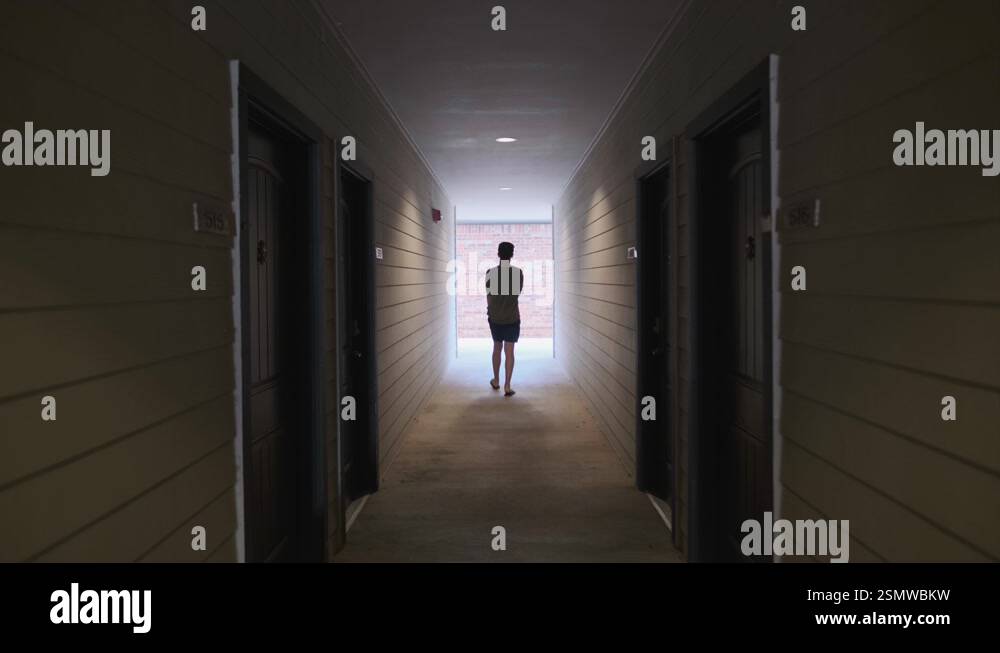 Rear view of young man carrying box through apartment building hallway ...