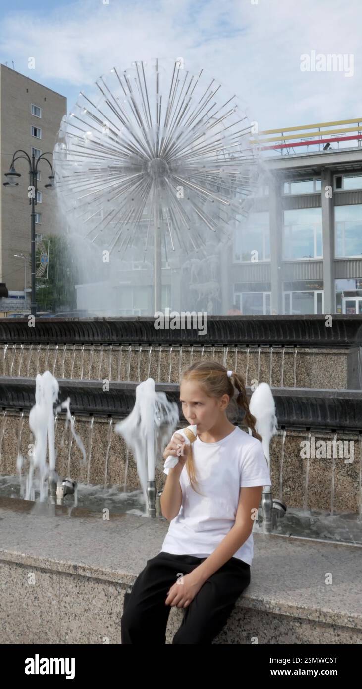 Fountain in the shape of a dandelion. A teenager girl eating ice cream ...