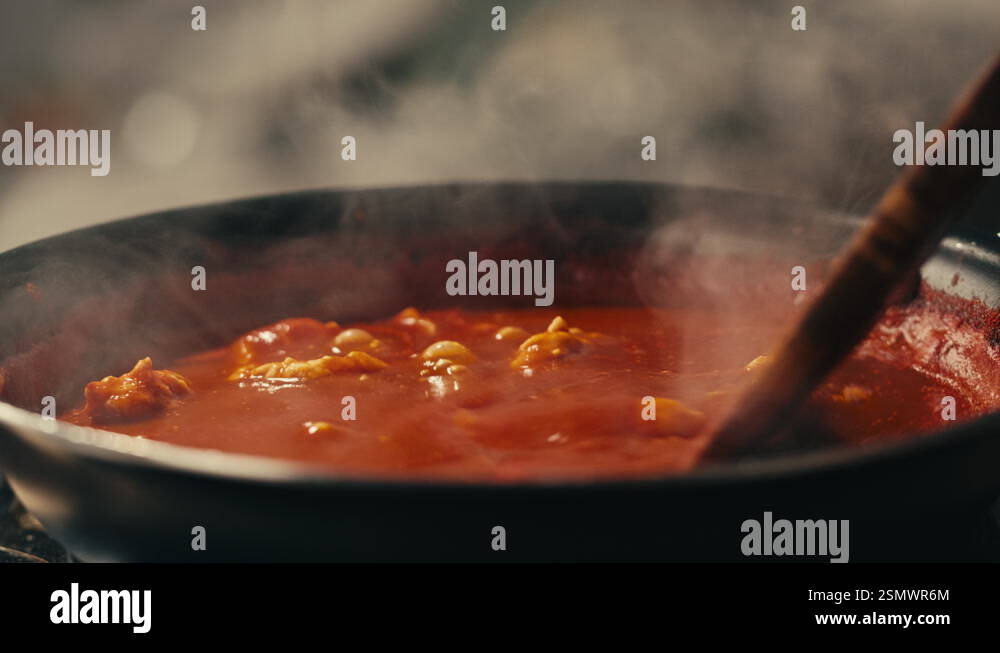 Chicken in tomato sauce is boiling on a frying pan with spices. Cooking ...