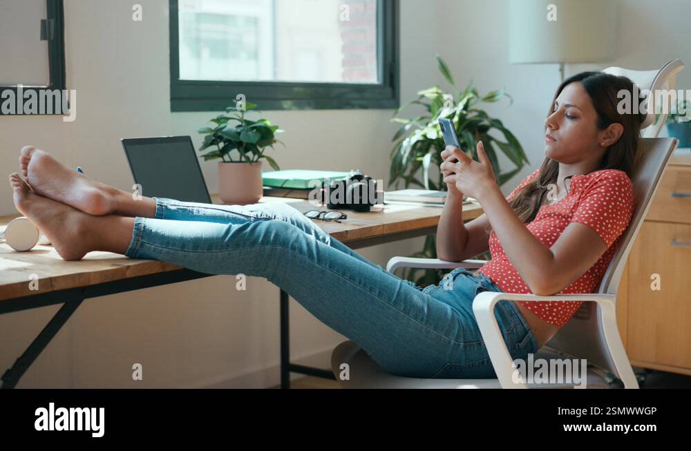 Businesswoman sitting at desk with feet up reading text messages Stock ...