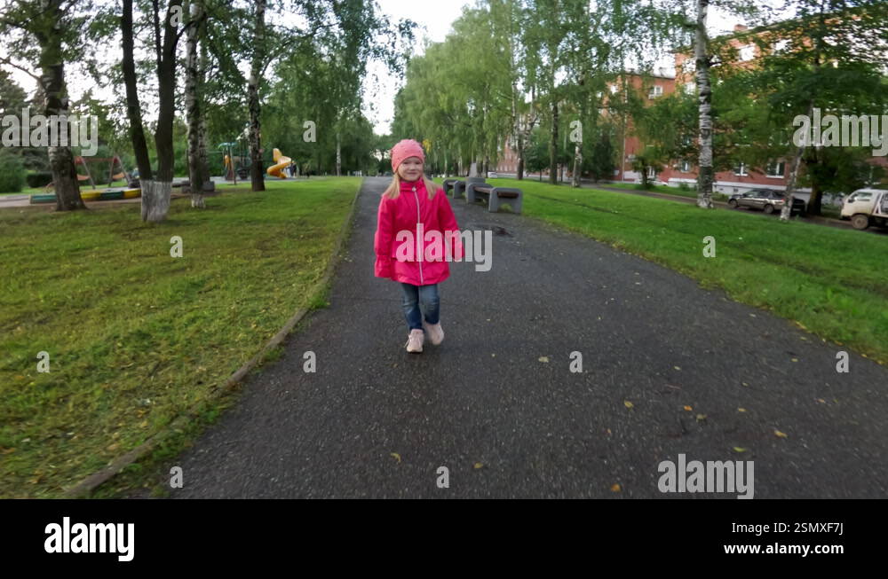 Young girl is happily running towards the camera on a paved pathway in ...