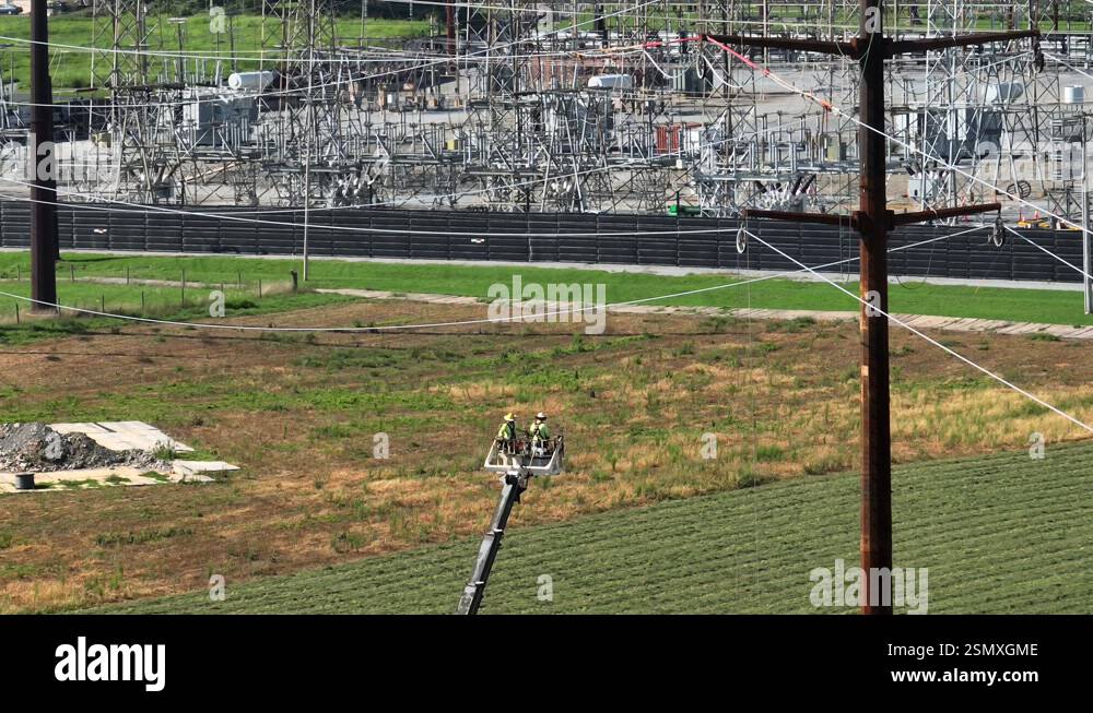 Linemen in lift repairing wire of electricity pylon in front of ...