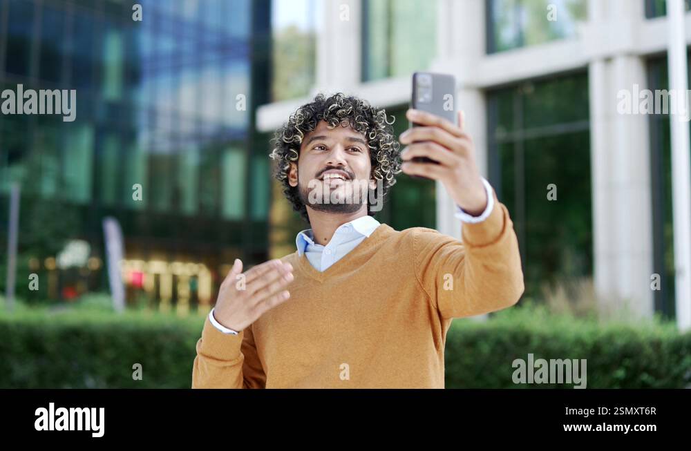 Smiling young man making video call outside modern office building ...