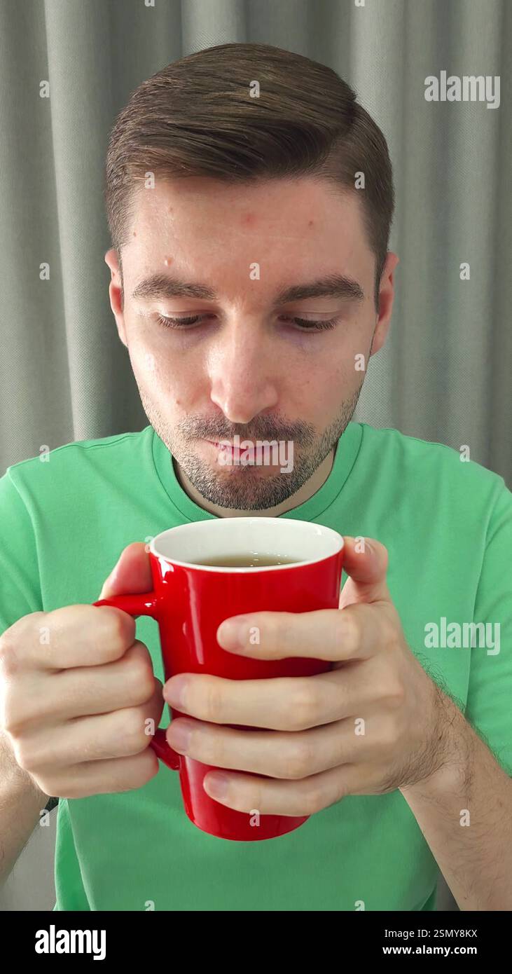 Man holding a red mug with both hands and sips a tea or coffee ...