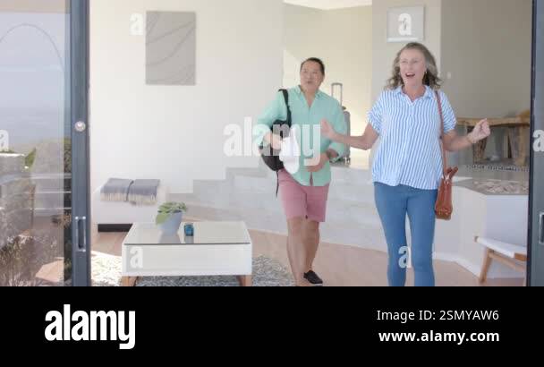 Senior couple arriving home from vacation, smiling and holding hats ...