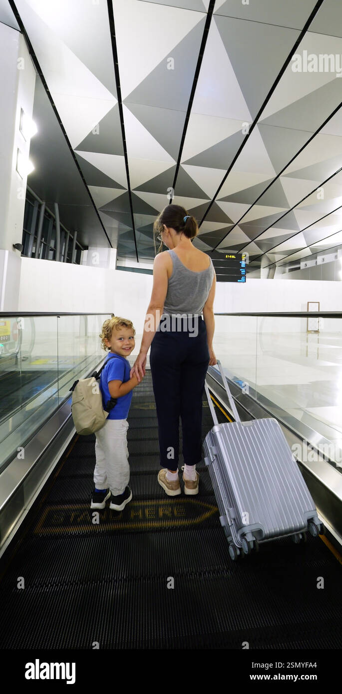 Little son stand on travolator with mother, cute glance back to camera ...