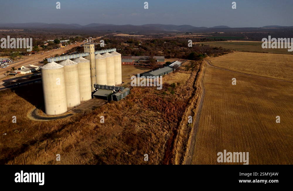 Aerial pan view of grain tower silos next to vast farm land in dry ...