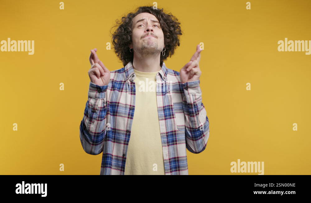 Handsome man praying. crossed fingers, yellow background.Guy begs ...