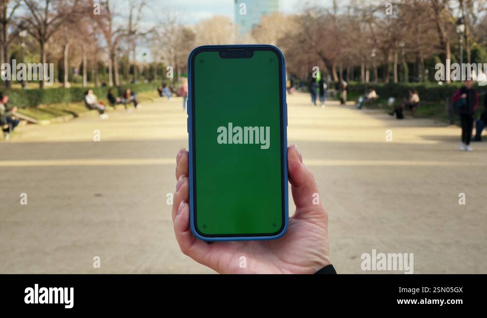 Close up of phone with vertical green screen in hands on city park ...