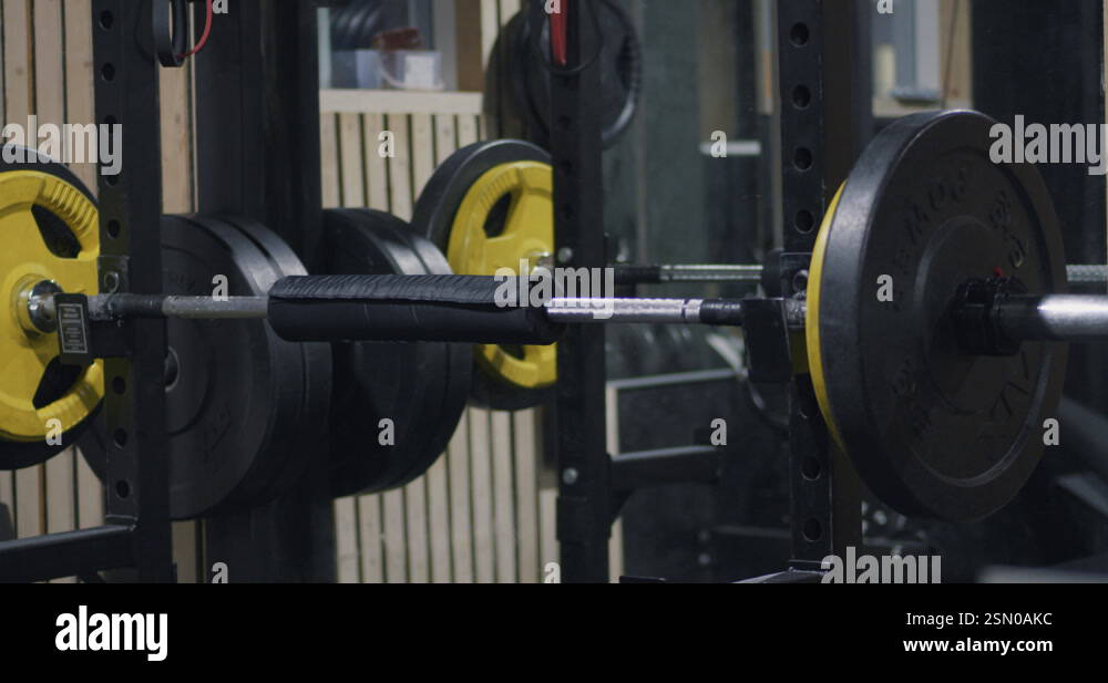 Barbell loaded with weight plates on a rack in a gym setting ready for ...