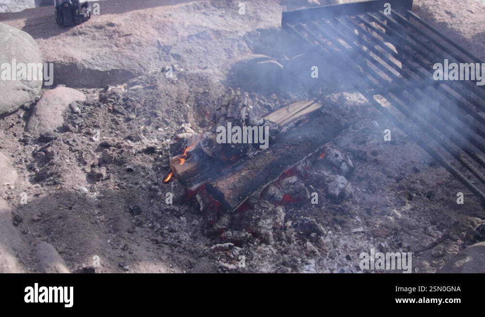 A campfire burns down in an outdoor setting with smoke rising and ...