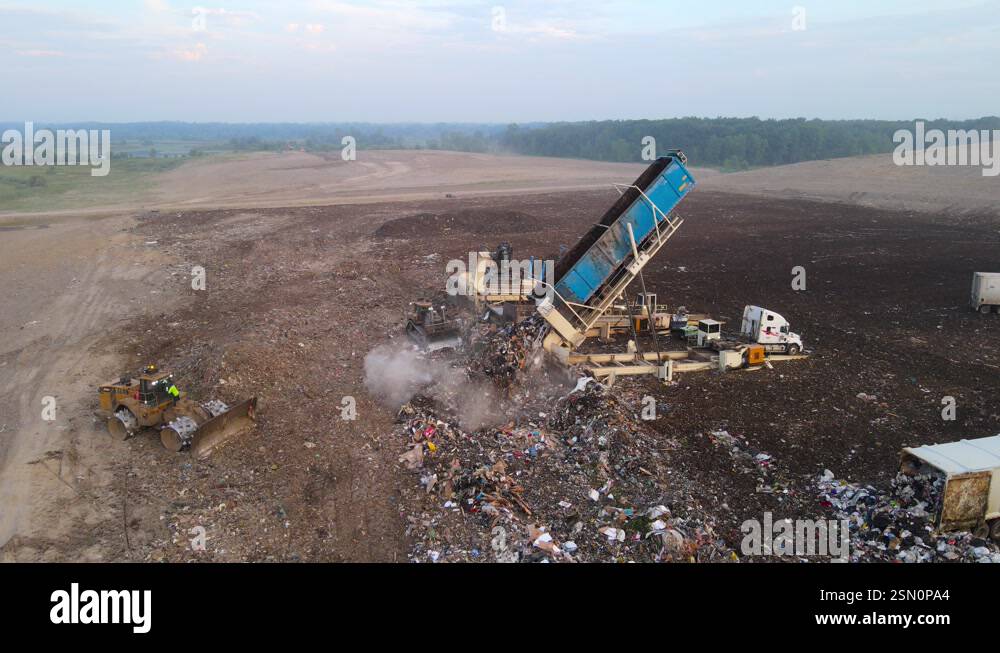 Landfill site with trucks and machinery dumping and spreading waste in ...