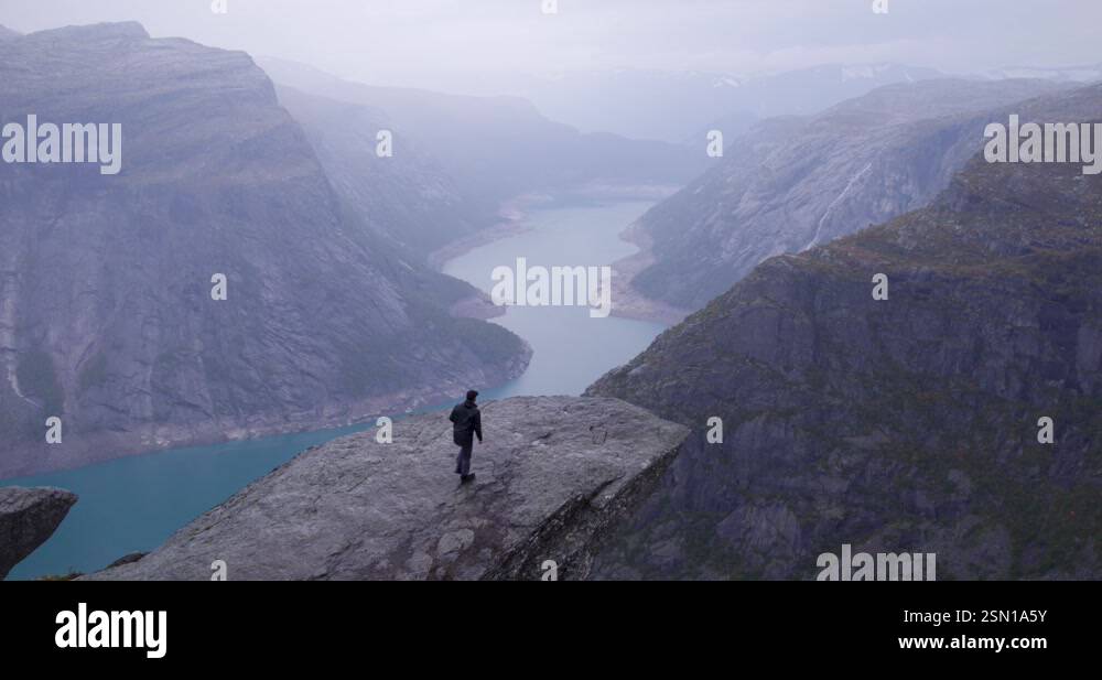 Trolltunga mountain in Norway with guy walking out watching the fjord ...