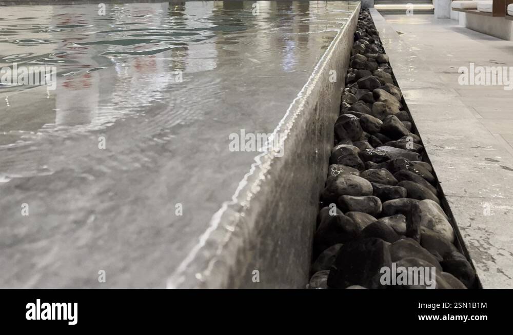 Water from infinity pool spilling over into black rocks, close up Stock ...