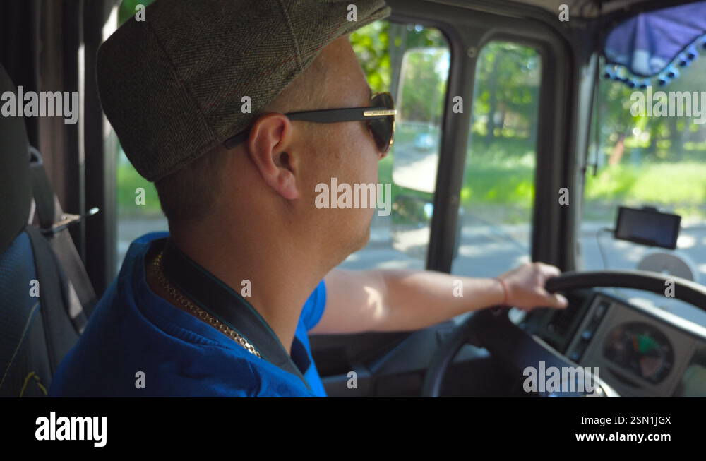 Profile of lorry driver inside cabin riding on city road and enjoying ...
