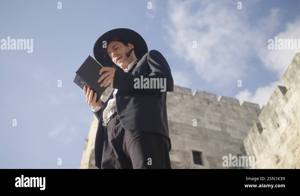 Pan shot of an Orthodox male in a black suit and hat, praying and ...