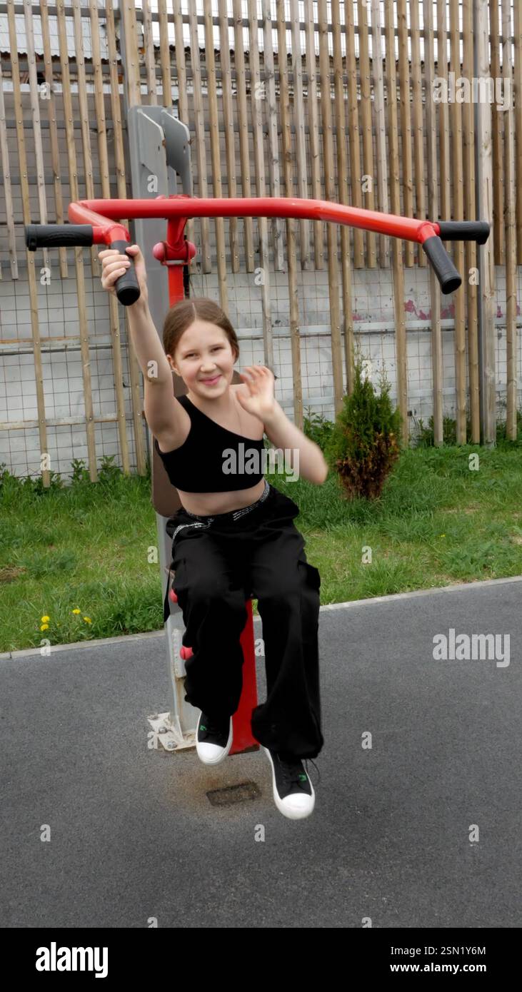 Teenage girl doing arm exercise in outdoor gym. Child training outside ...