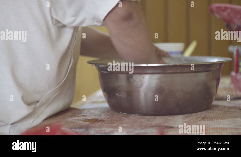 Close-up of a pastry chef vigorously mixing dough in a large metal bowl ...