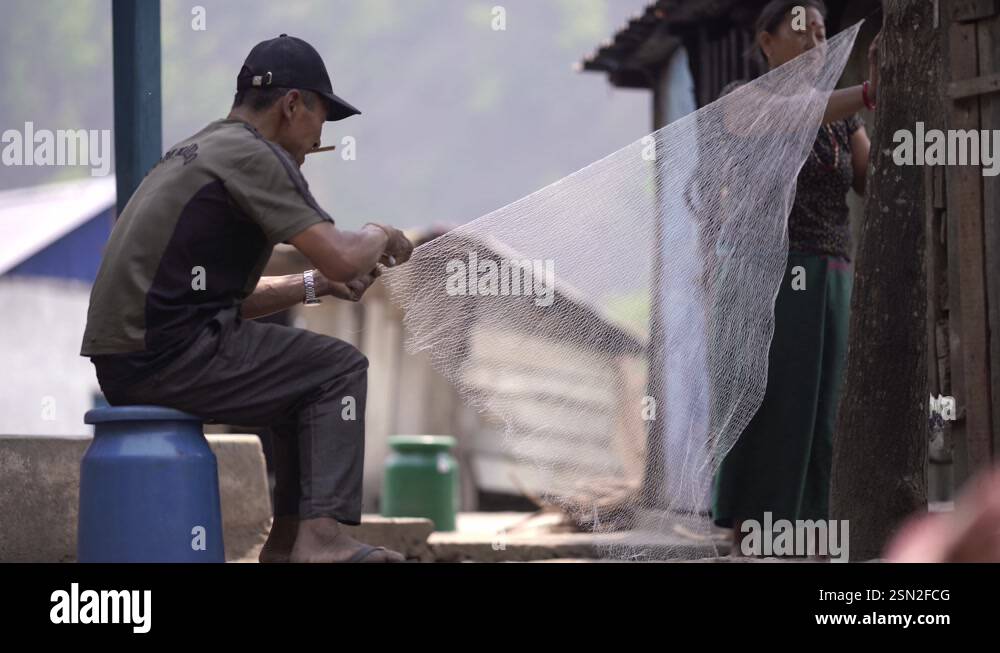 Close-up of a man weaving a traditional fishing net by hand in a Nepali ...