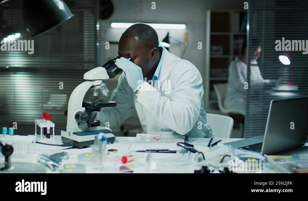 Forensic Scientist Using Microscope and Taking Notes in Crime Lab Stock ...