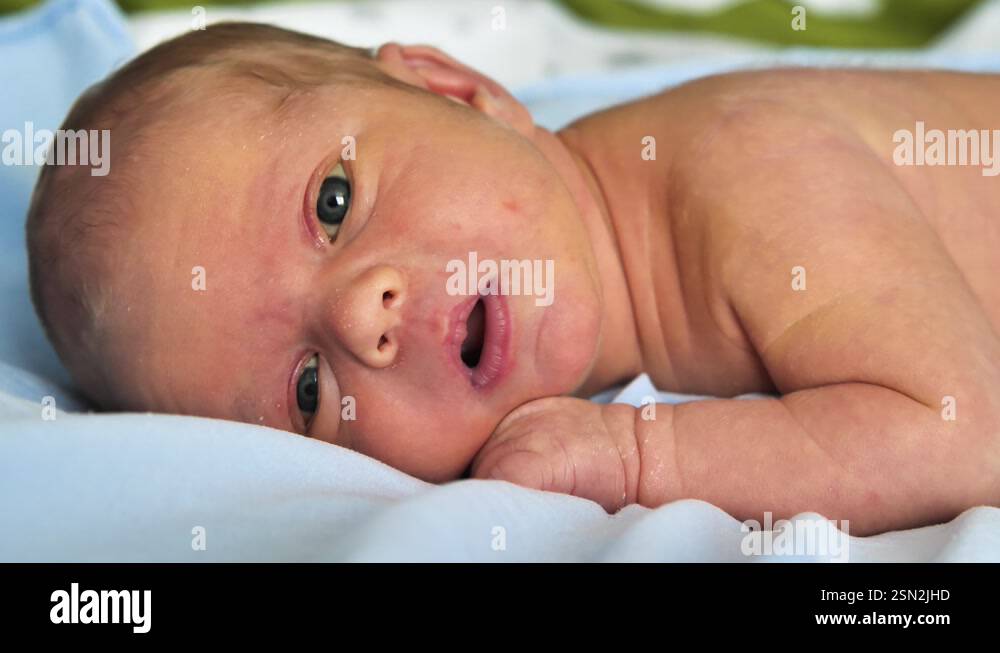Close-up of a newborn baby's head lying on a blue sheet with its mouth ...