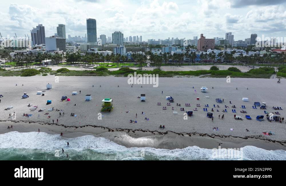 South Beach shoreline with beachgoers and umbrellas. Miami skyline in ...
