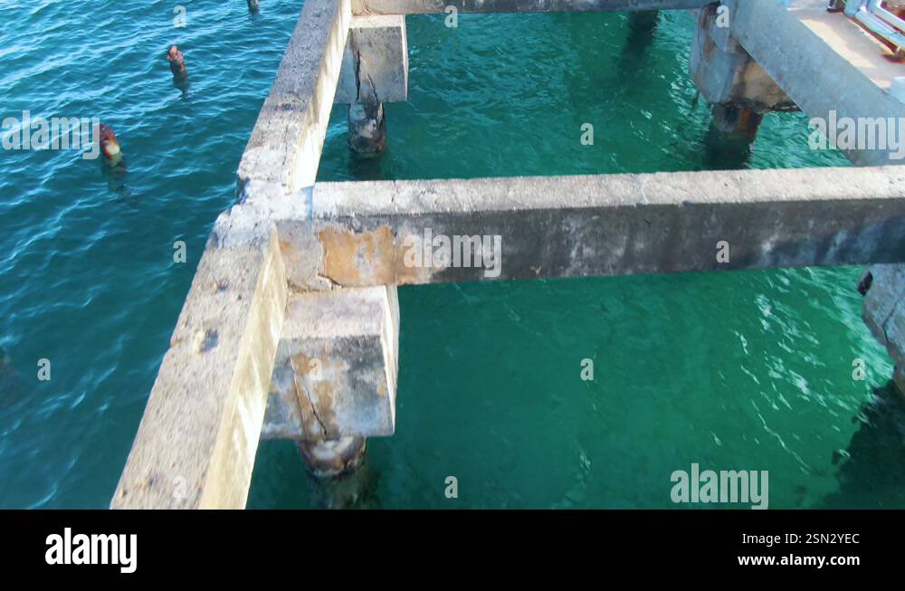 An overhead aerial flyover of a worn-down concrete pier pans up to ...