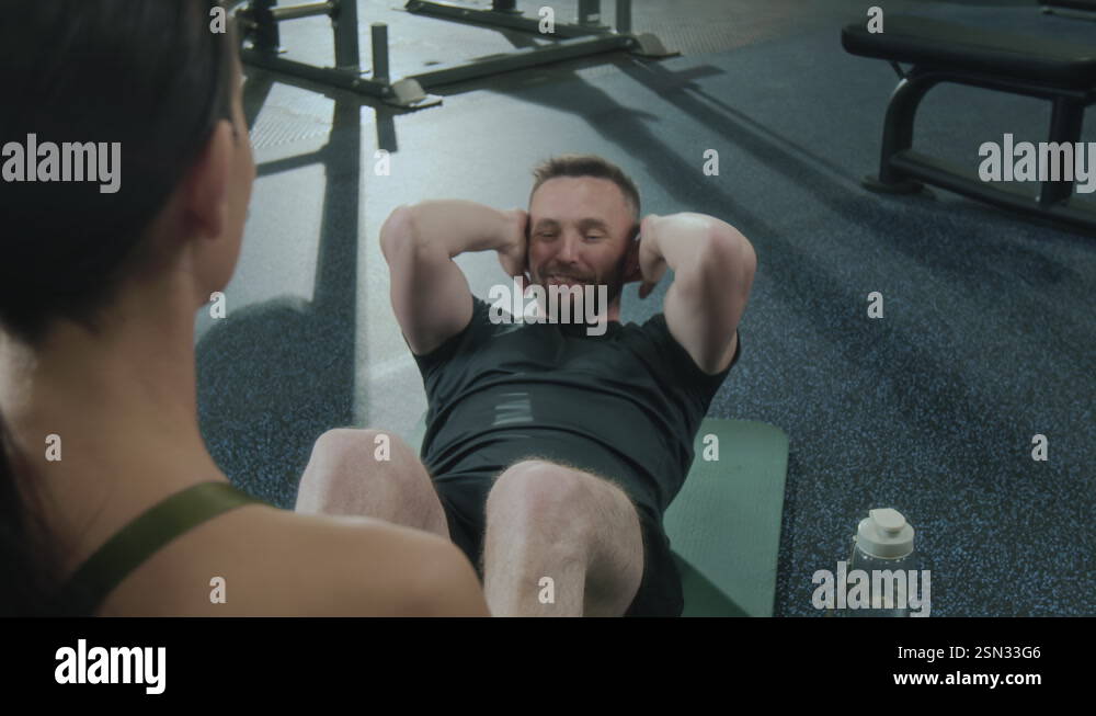 Man Performing Sit Ups with Help of Female Training Partner in Gym ...