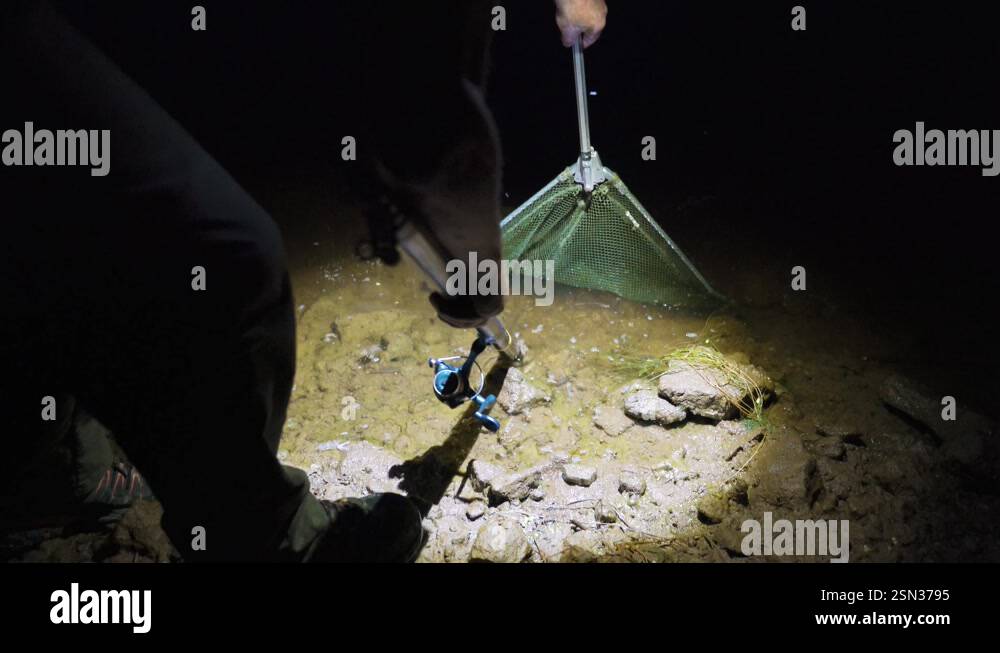 Catching small fish by the river coast at night with a net in hands ...